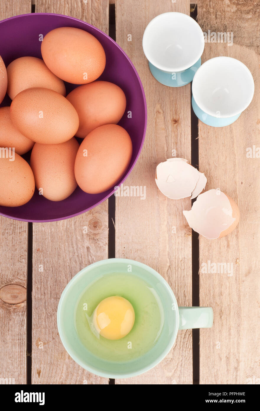 Nine hen's eggs in purple bowl on picnic table next to fresh raw egg in ...