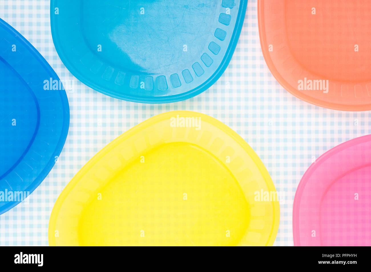 Colourful plastic plates on blue and white checked background, overhead ...