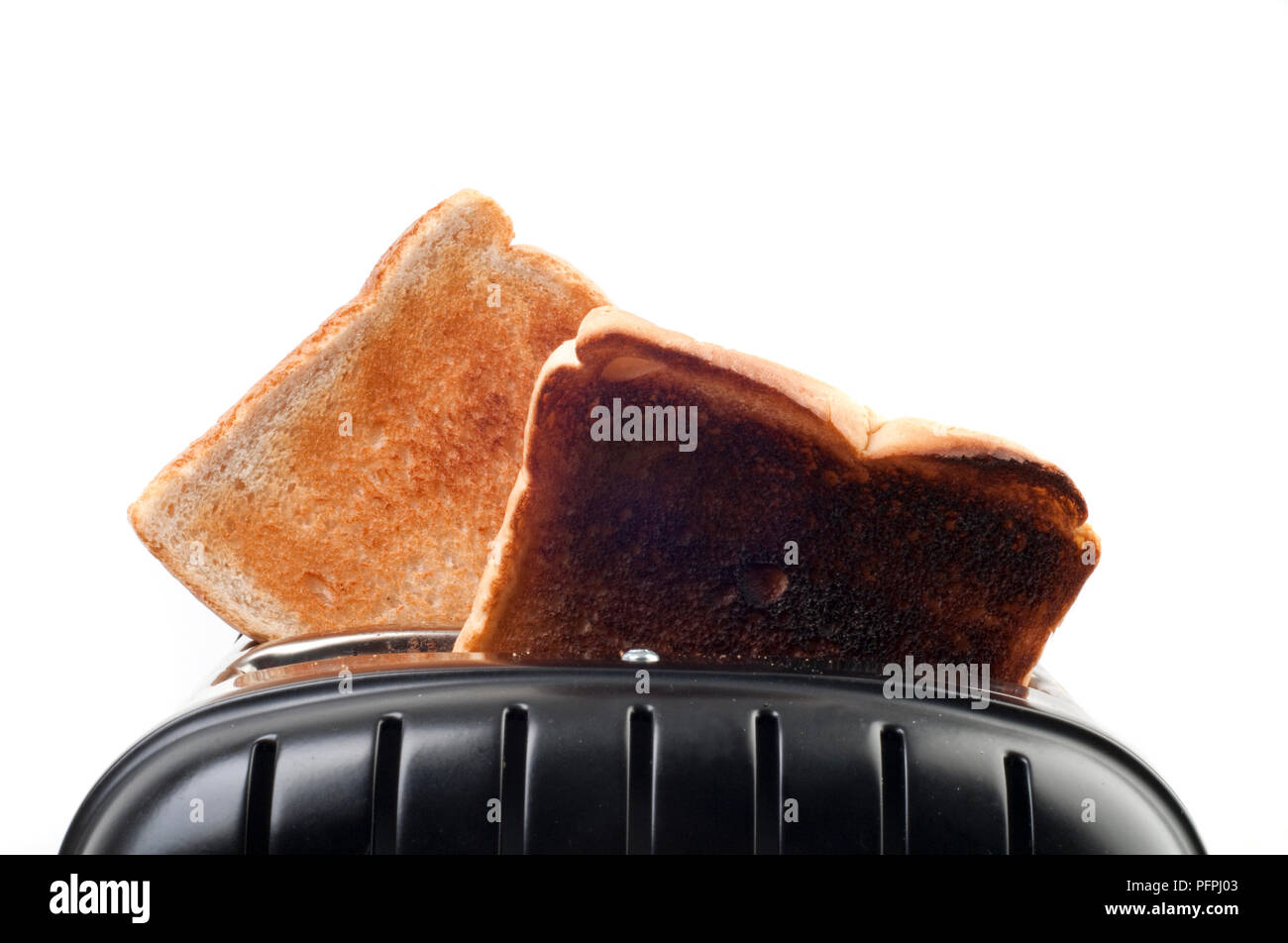Two slices of toasted white bread, one slice is burned, in toaster on ...
