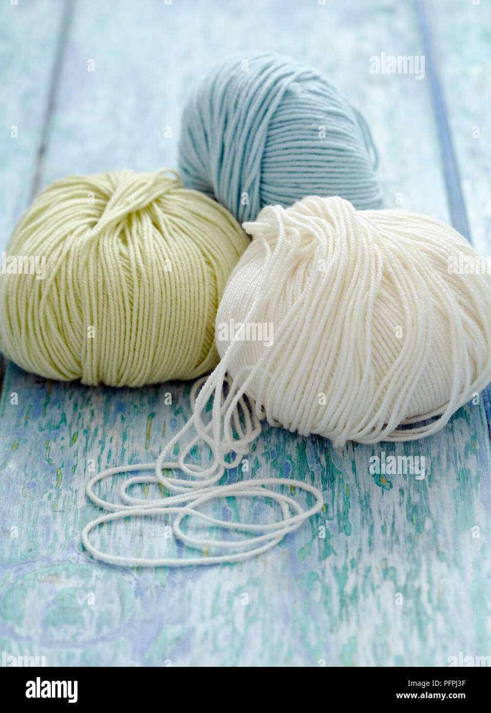 Three balls of wool, blue, light green and white, on blue wood ...