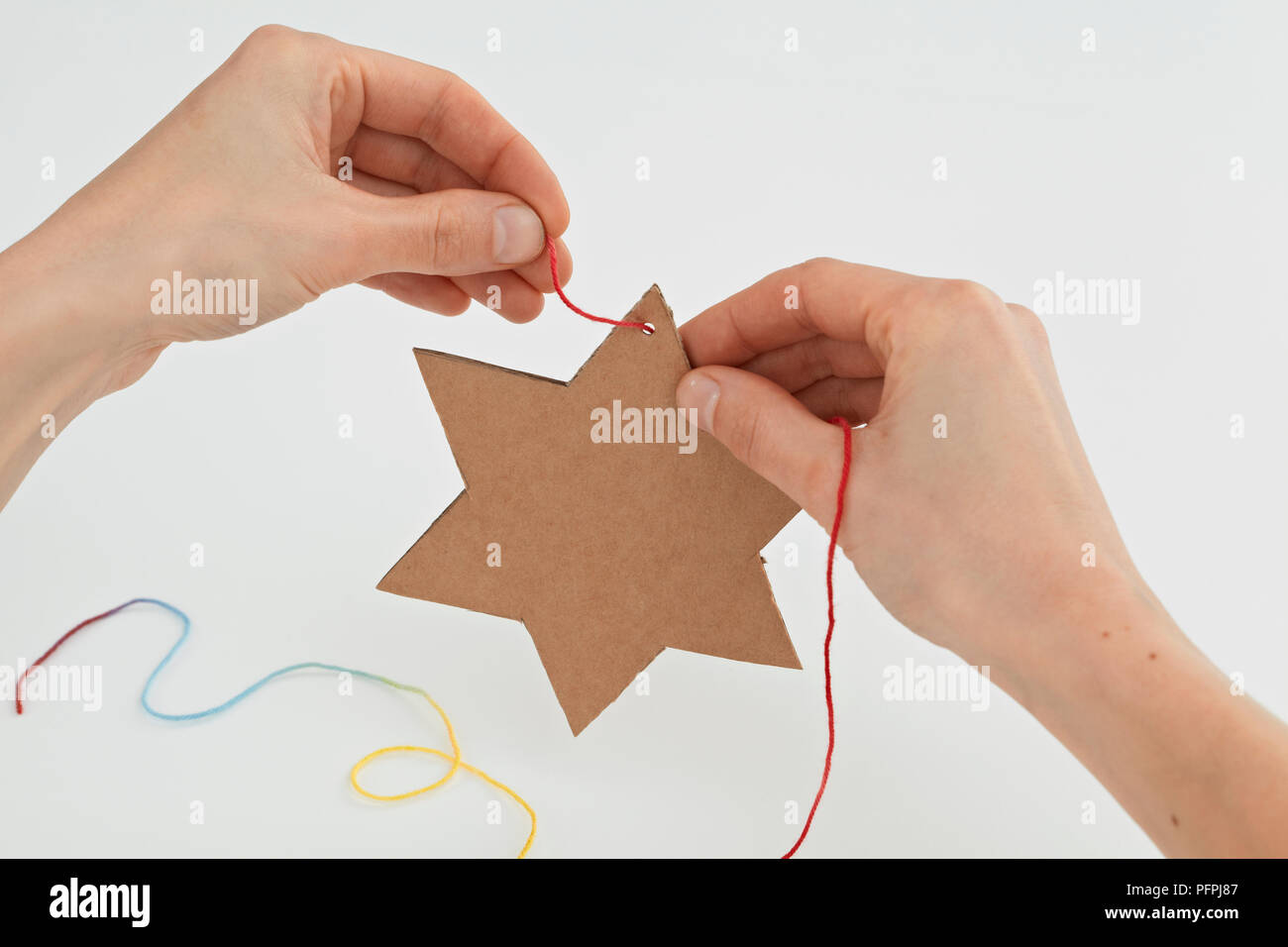 Threading coloured string through cardboard star, close-up Stock Photo ...