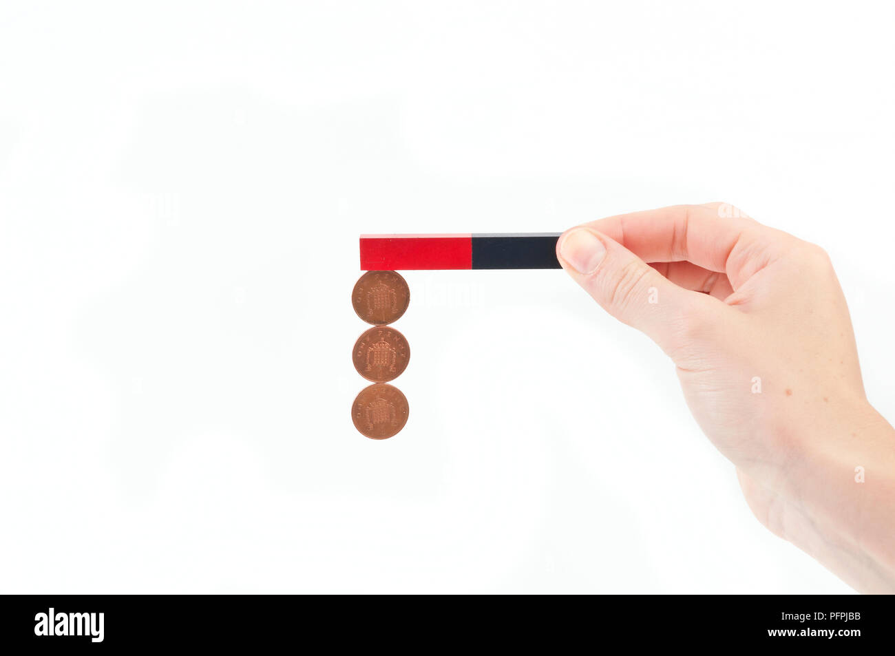 Hand holding bar magnet with three coins attached at one end Stock ...