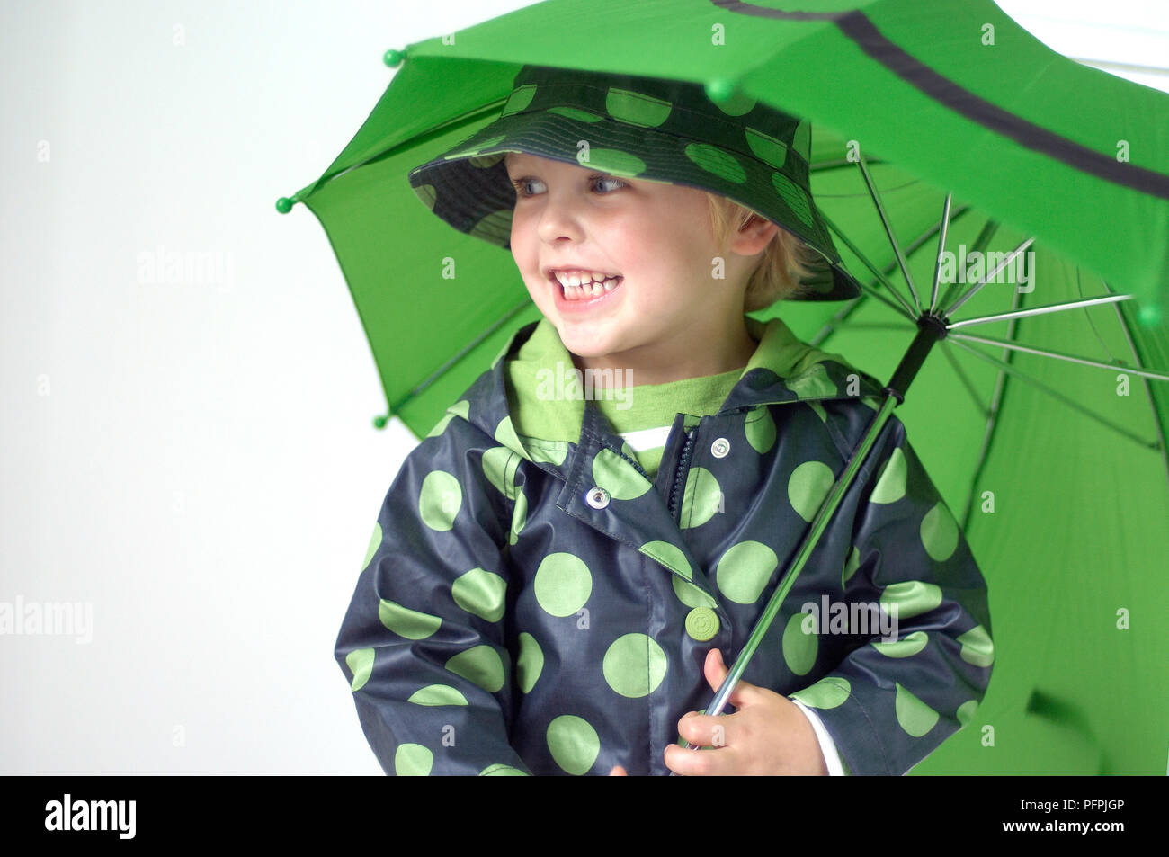 Boy wearing green spotty raincoat and hat, holding green umbrella ...