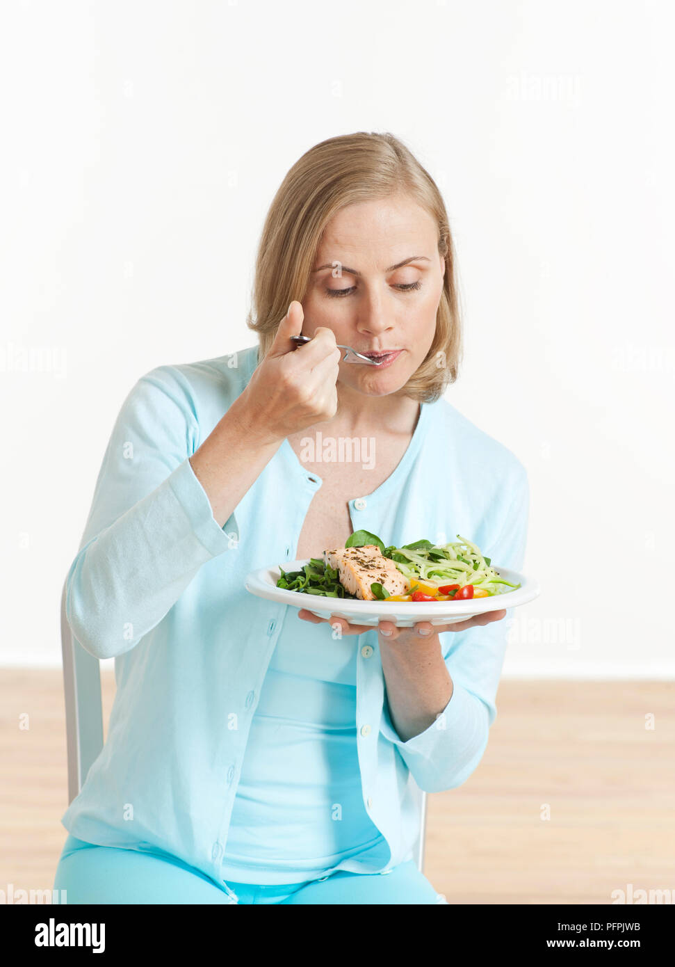 Woman sitting on chair eating salmon salad balanced on hand Stock Photo ...
