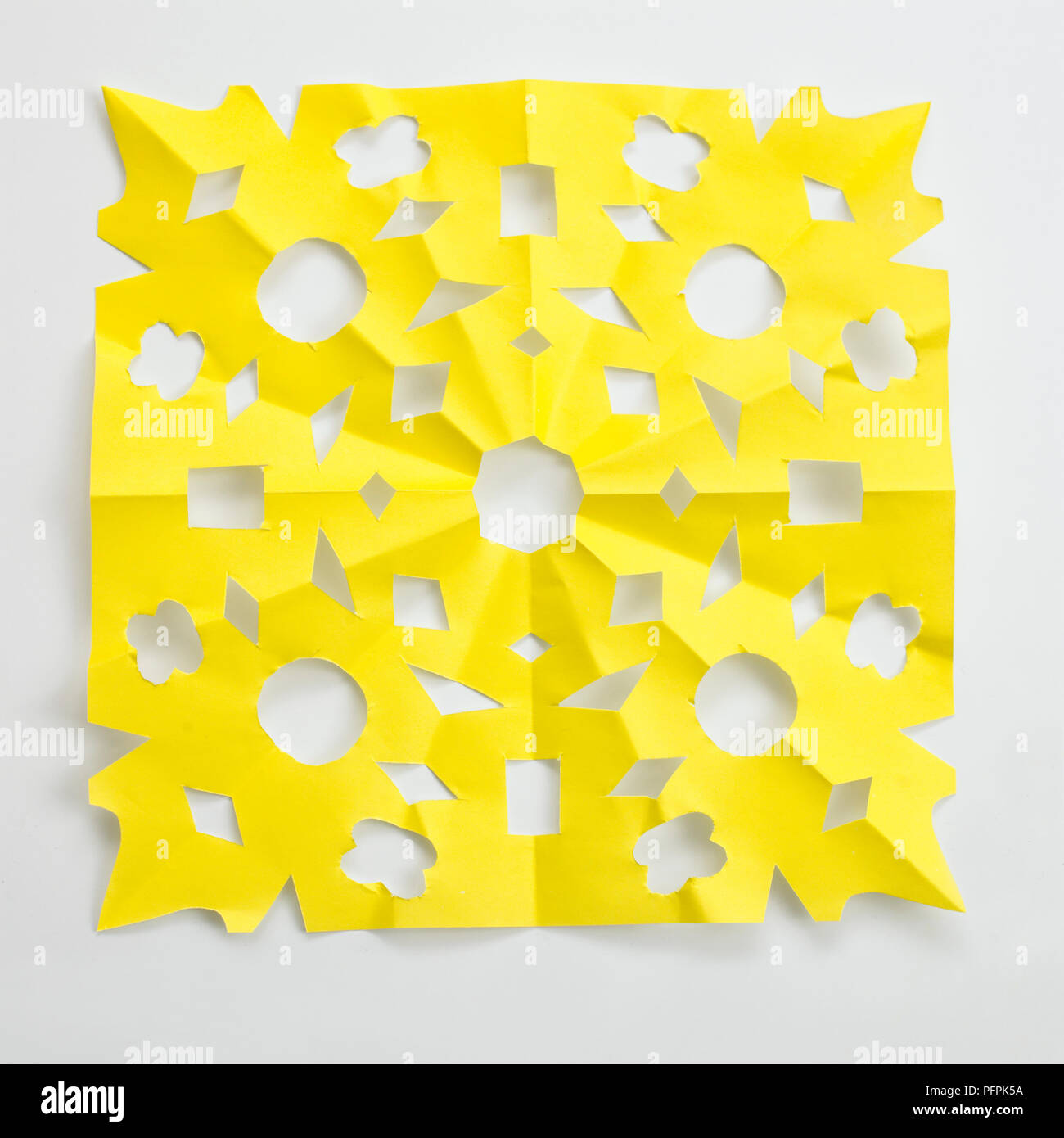 Yellow piece of paper with symmetrical pattern cut into it Stock Photo ...