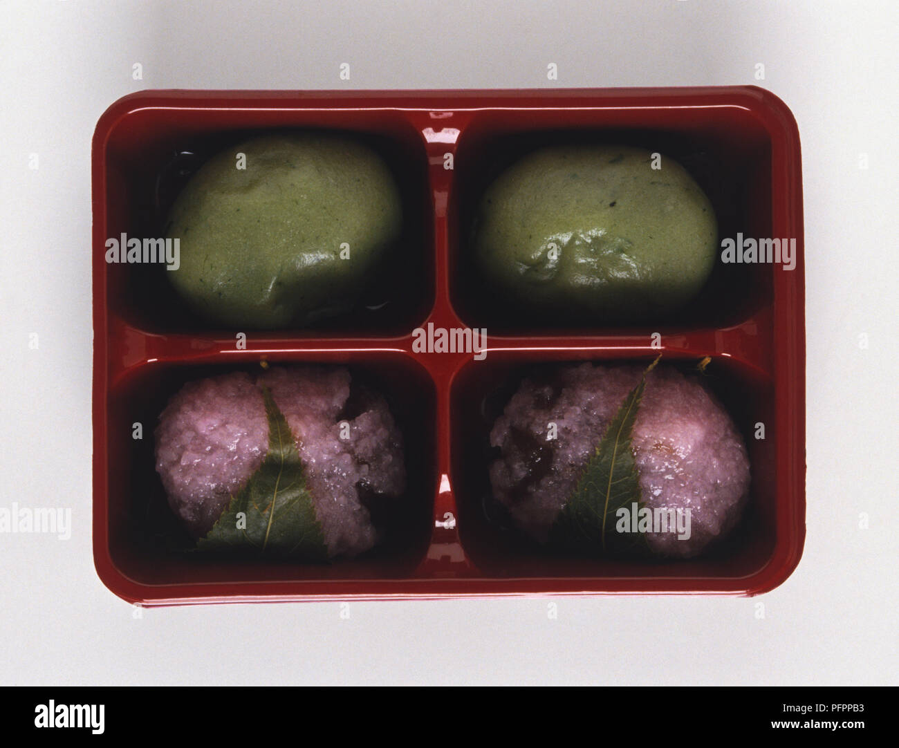 Pink rice cakes wrapped in cherry leaves in a tray viewed from above ...