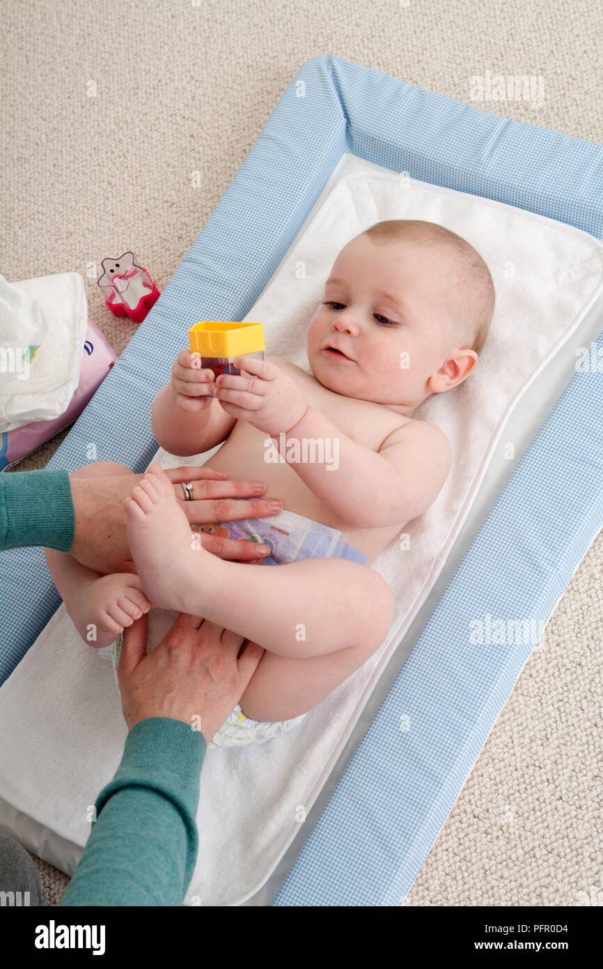 Baby boy playing with toy while having his nappy changed Stock Photo ...