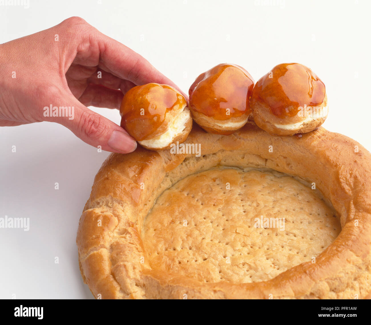 Placing glazed choux pastry balls around the edge of a cake base Stock ...