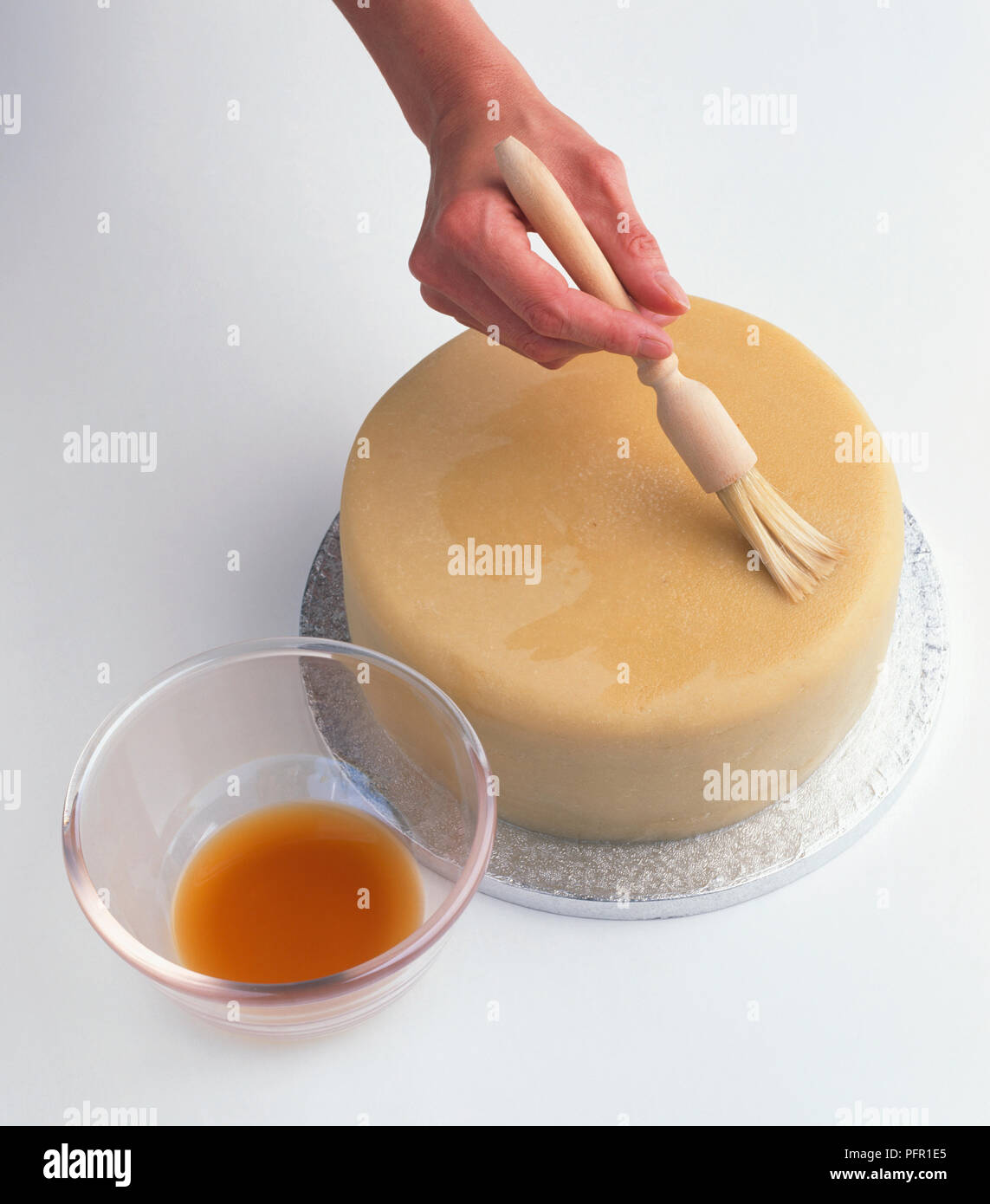 Person using basting brush to moisten cake topped with marzipan with ...