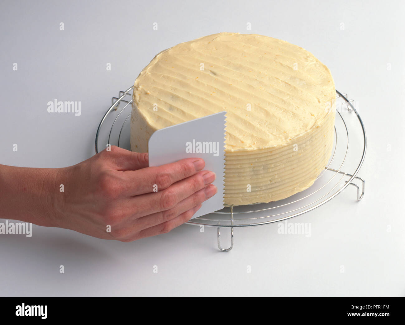 Decorating a layered sponge cake by passing comb over buttercream Stock ...