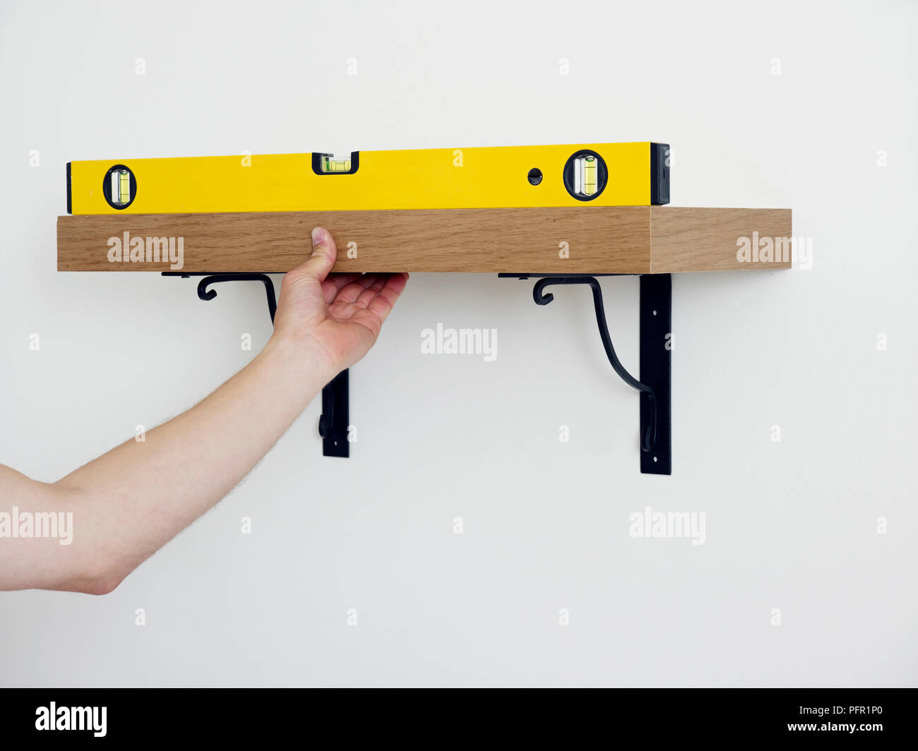 Man holding spirit level on shelf attached to white wall, close-up ...