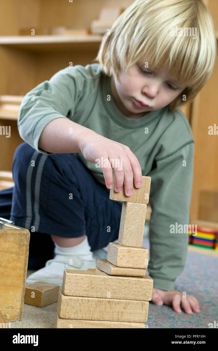 Blonde-haired boy sitting on floor, stacking wooden blocks Stock Photo ...