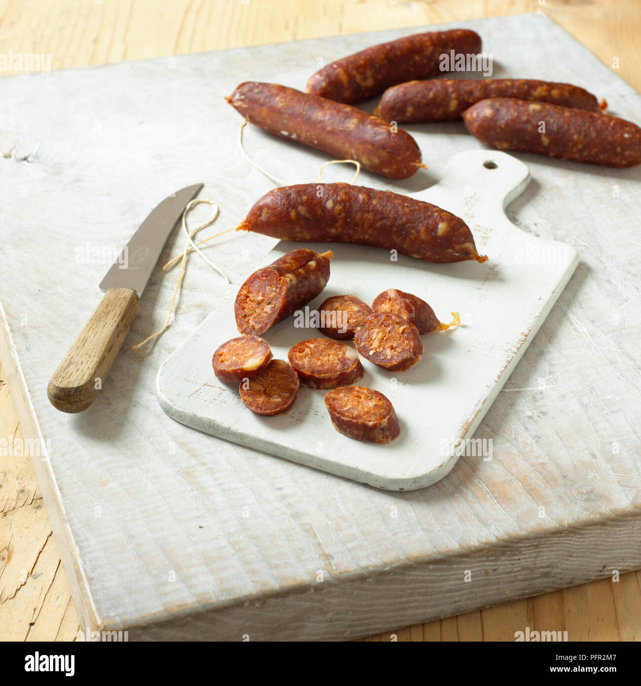 Whole and sliced Chorizo on chopping board with small kitchen knife ...