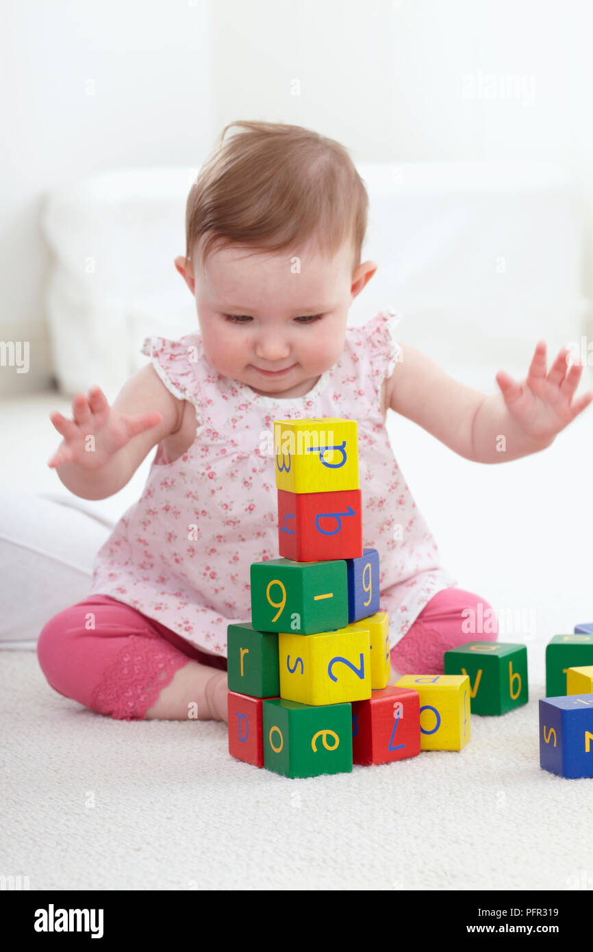 Baby girl (8.5 months) sitting behind a stack of wooden blocks with ...