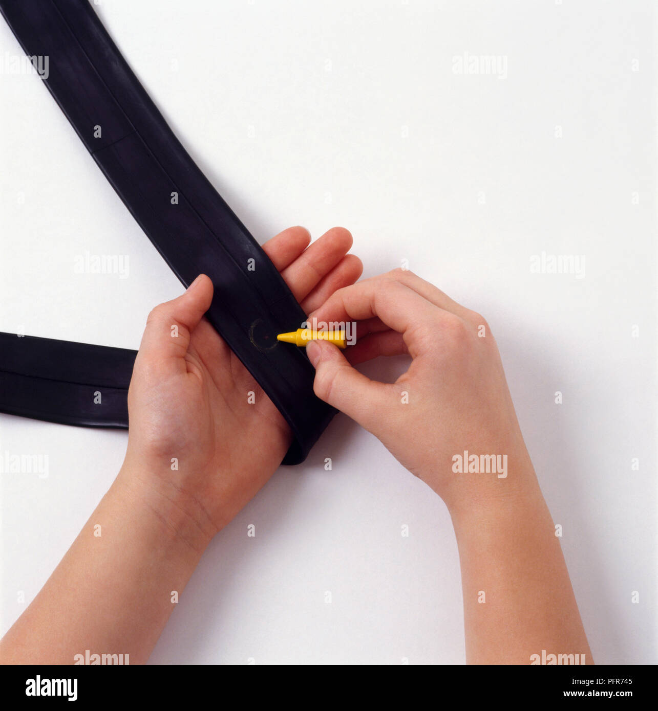 Boy marking puncture site on inner tube using yellow wax crayon, close ...