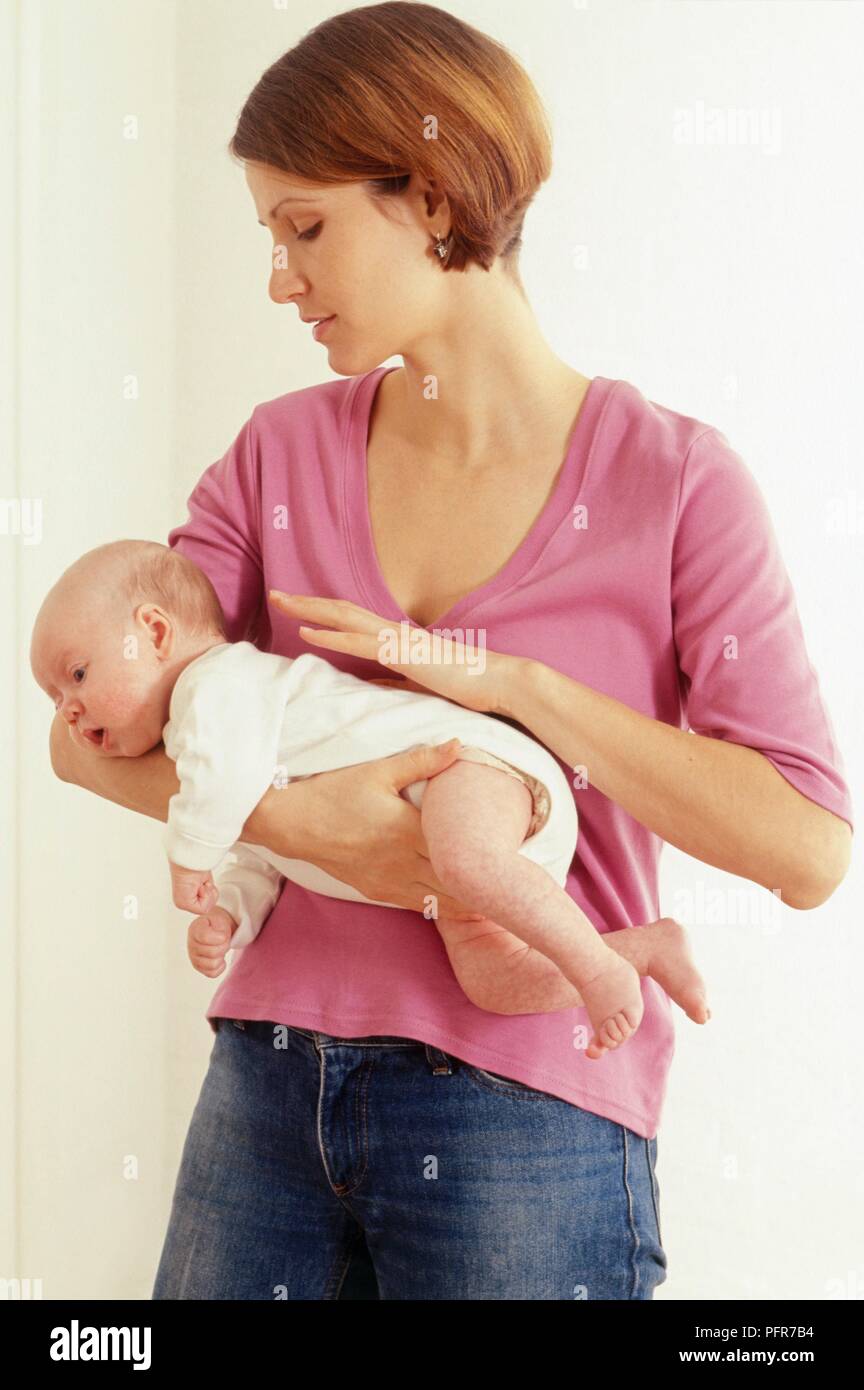 Woman holding newborn baby over her forearm while patting her back ...