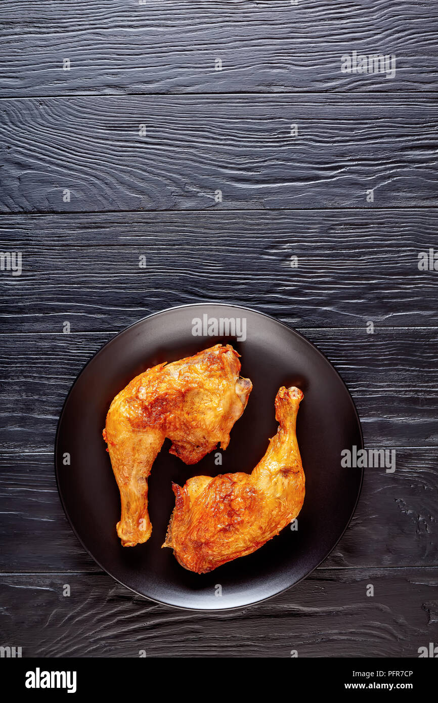 crispy fried chicken legs on a black plate on a wooden table, flat lay ...