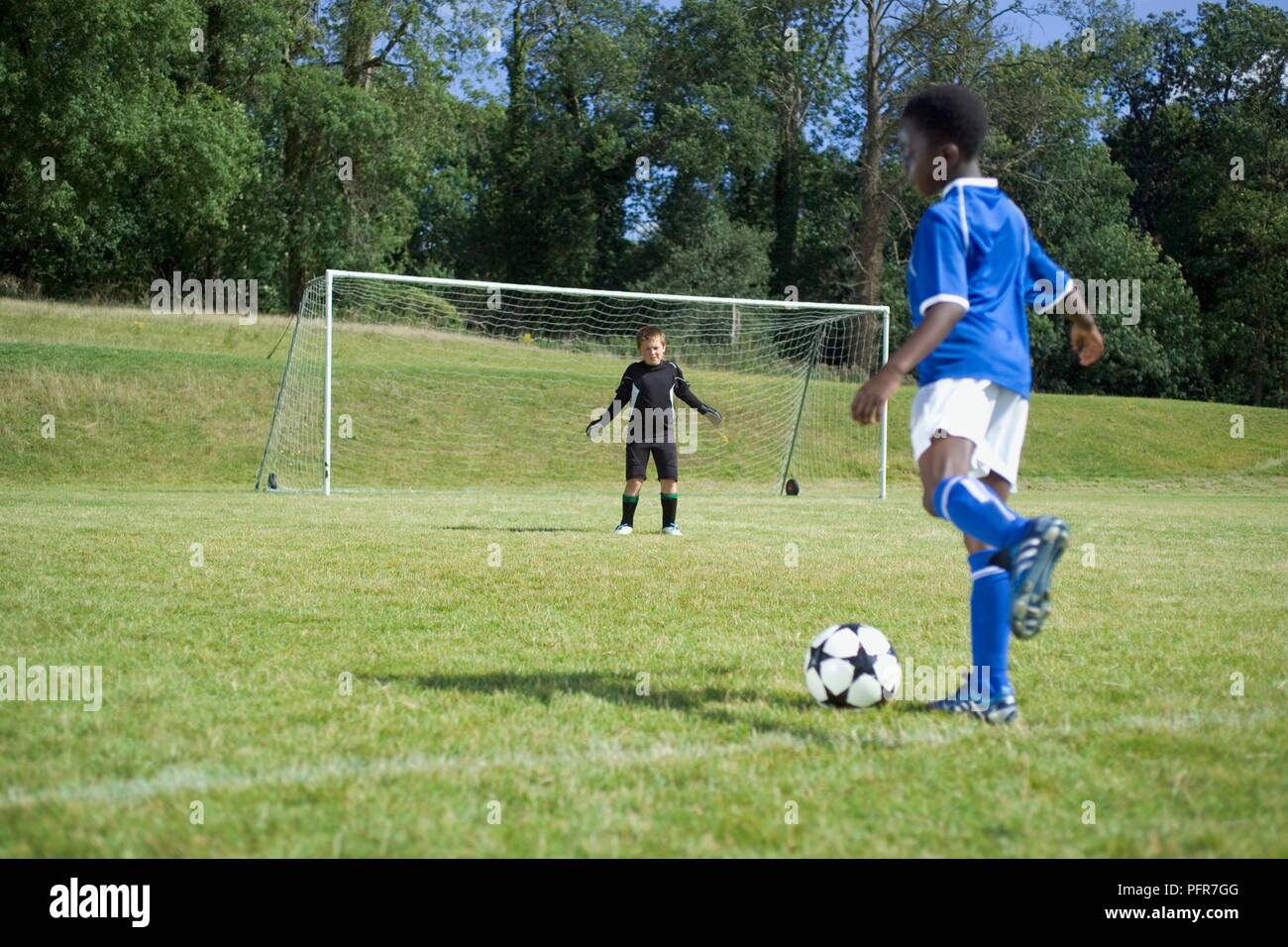 Young football player preparing to kick ball, goalkeeper standing ready ...