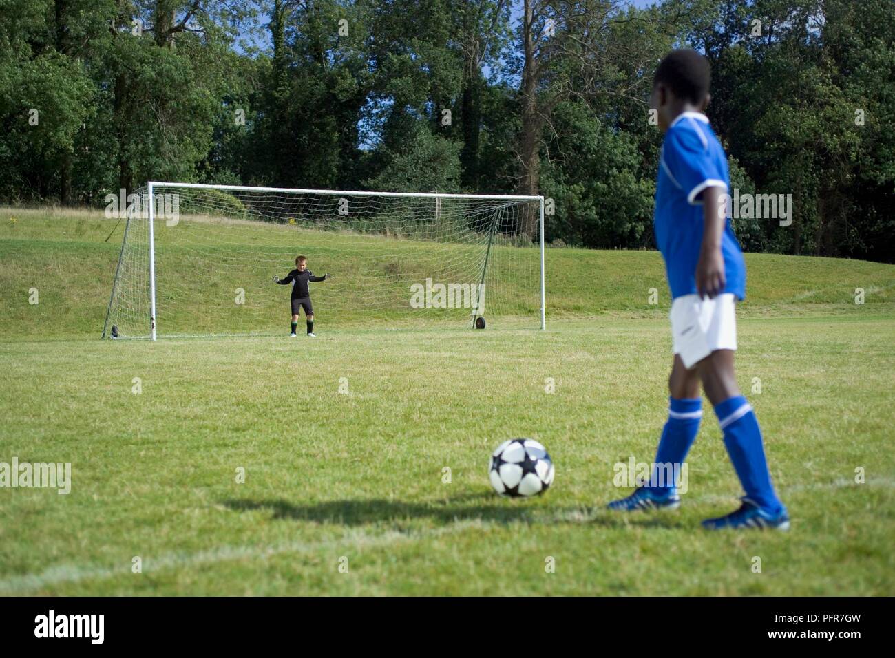 Young football player preparing to kick ball, goalkeeper standing ready ...