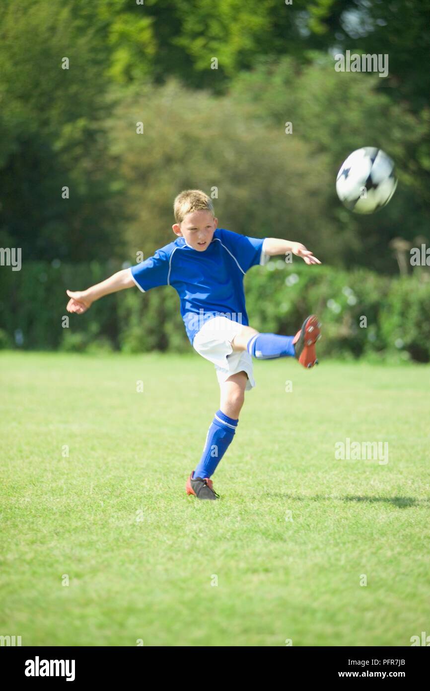 Young football player with his leg up in the air and ball in mid-air ...
