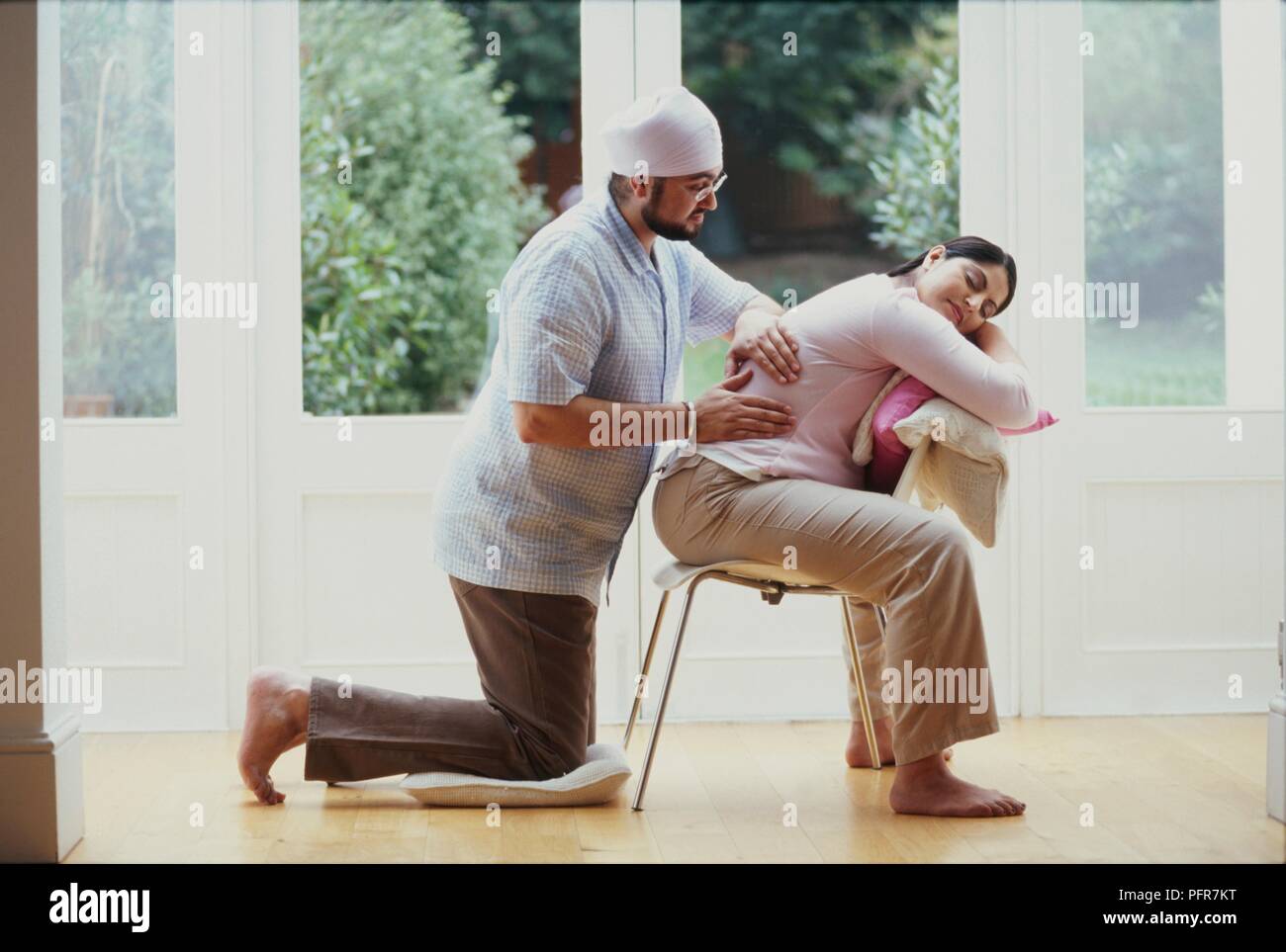 Pregnant woman seated on chair having her back massaged by man Stock ...