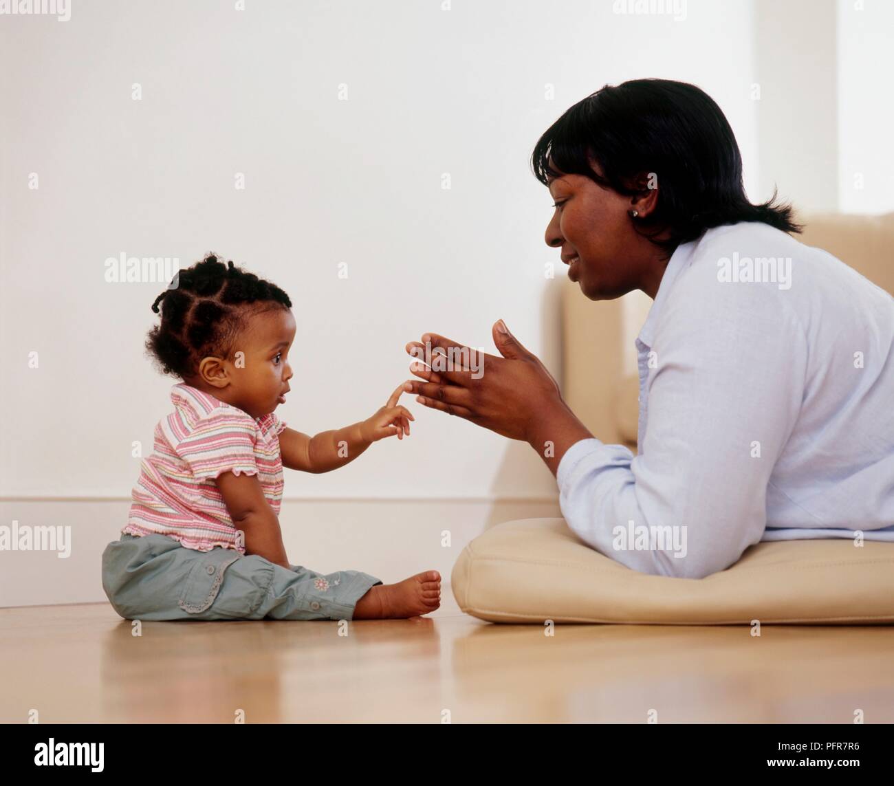 Baby girl sitting on floor touching woman's hands with her finger Stock ...