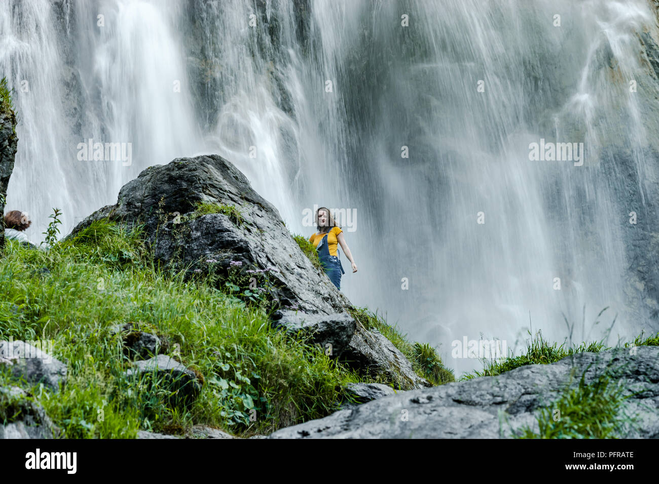 Young teenage girl standing on the big stone near waterfall, water ...