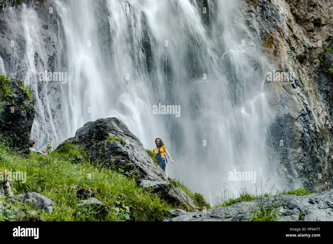 Young teenage girl standing on the big stone near waterfall, water ...