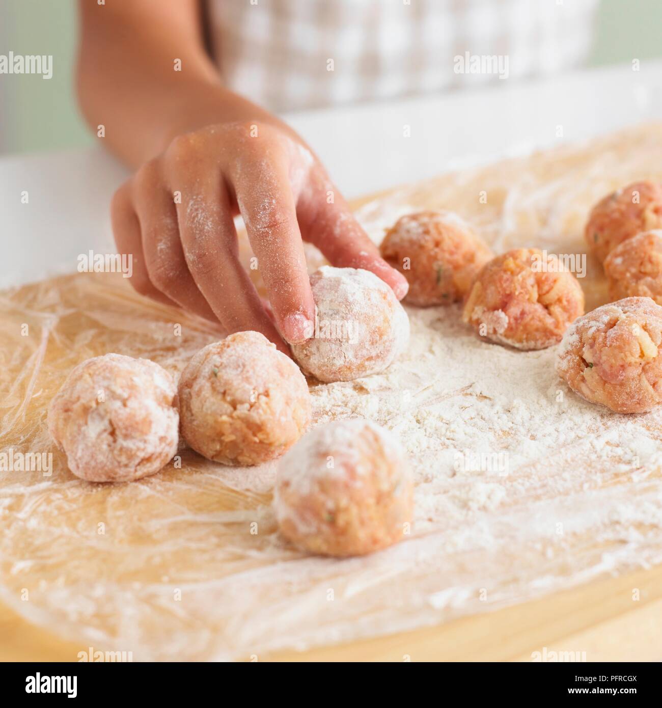 Child rolling meatballs in flour on wooden chopping board Stock Photo ...