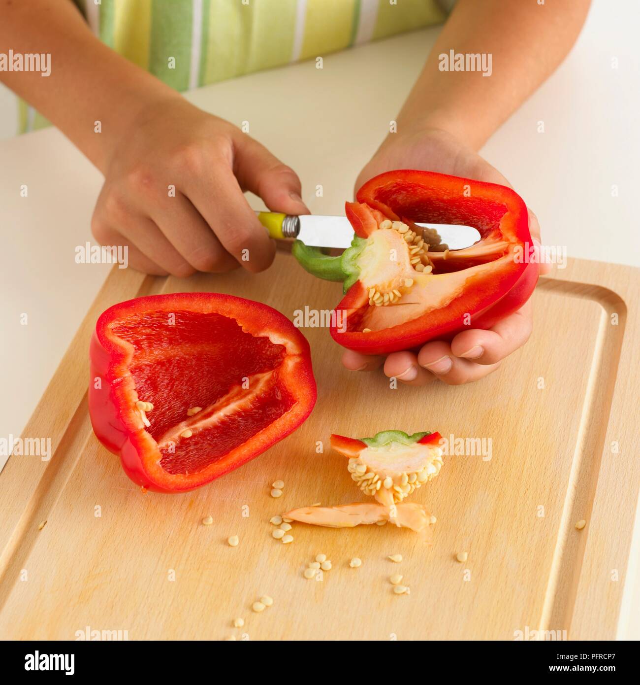 Girl's hands removing seeds from halved red pepper, using a knife ...