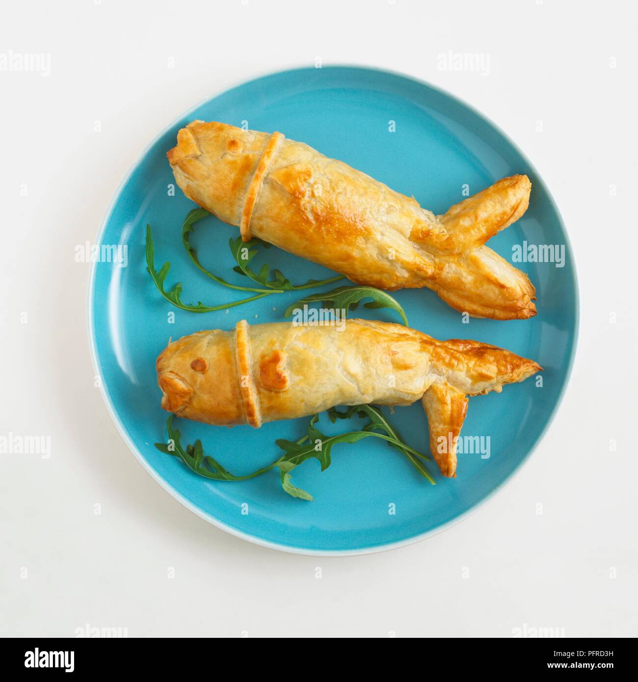 Fish-shaped puff pastry on a blue plate garnished with rocket leaves ...