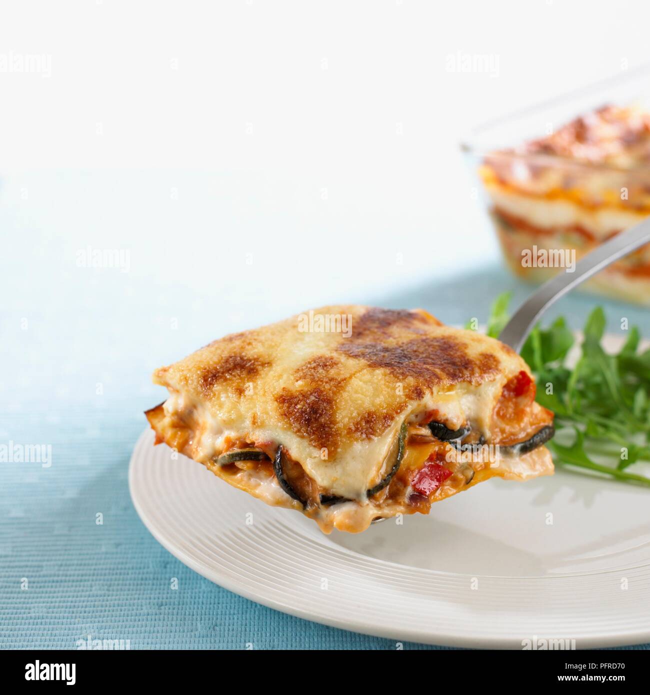 Serving of vegetable lasagne on a spatula, held above a plate, close-up ...