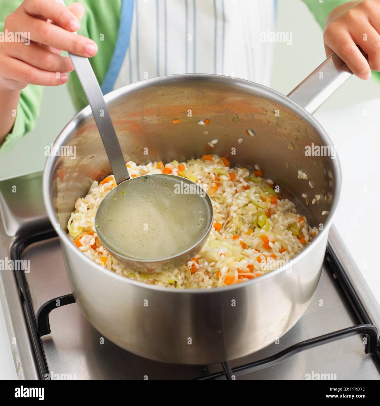 Girl adding stock to a vegetable risotto in pan, close-up Stock Photo ...