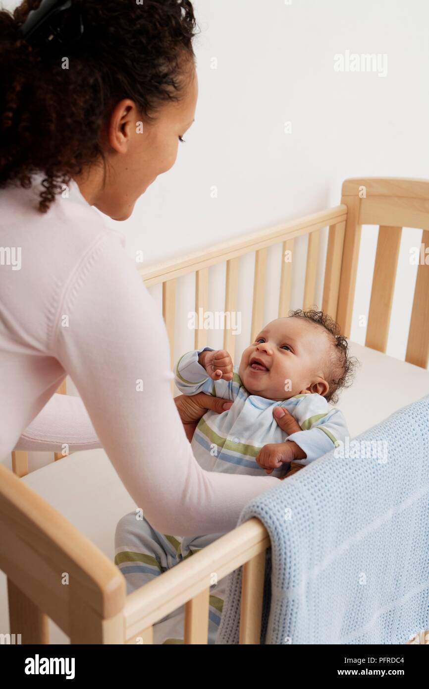 Woman picking up baby boy from cot Stock Photo - Alamy