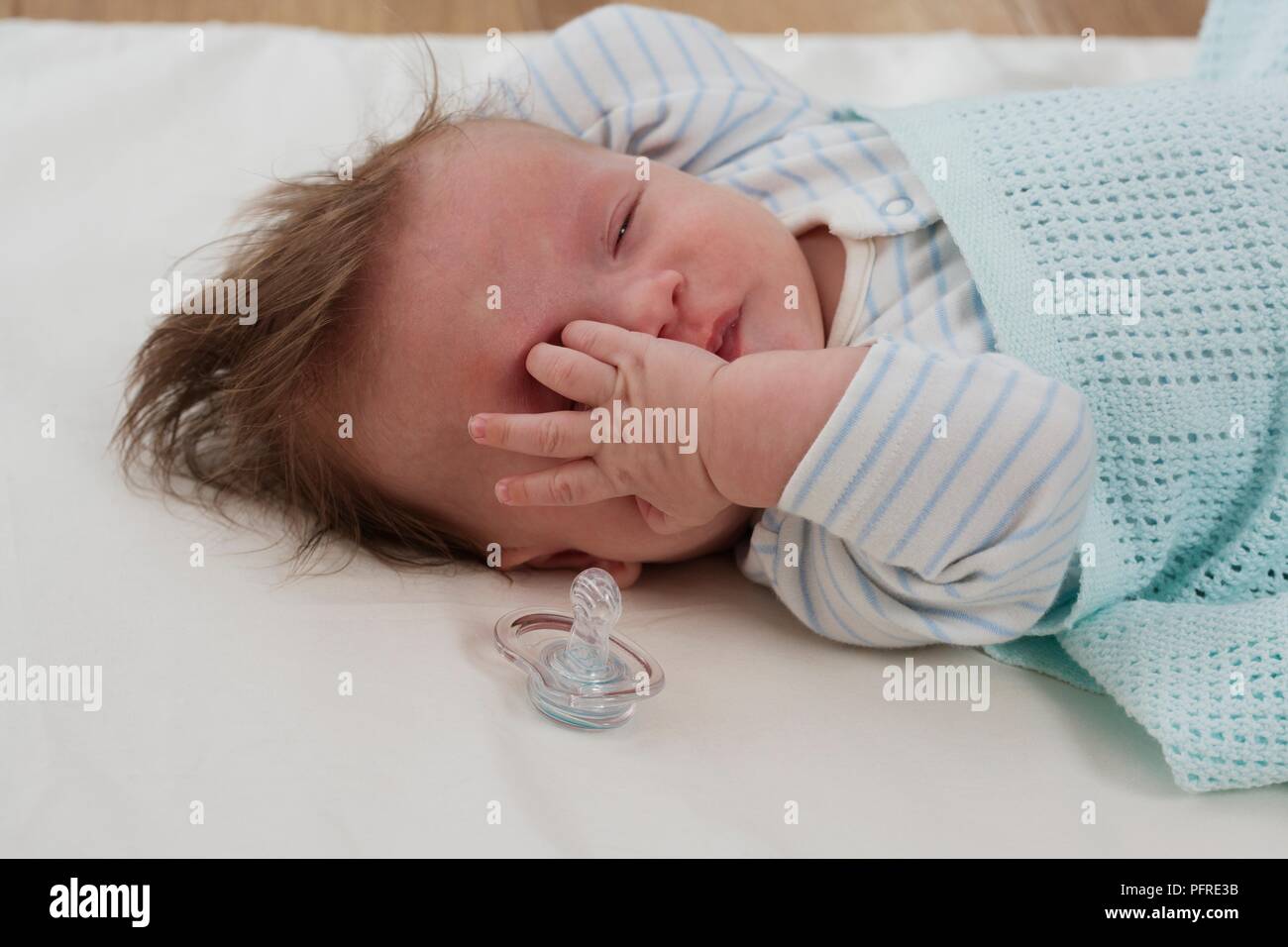 Baby boy lying on his back rubbing his eyes, dummy by his side Stock ...