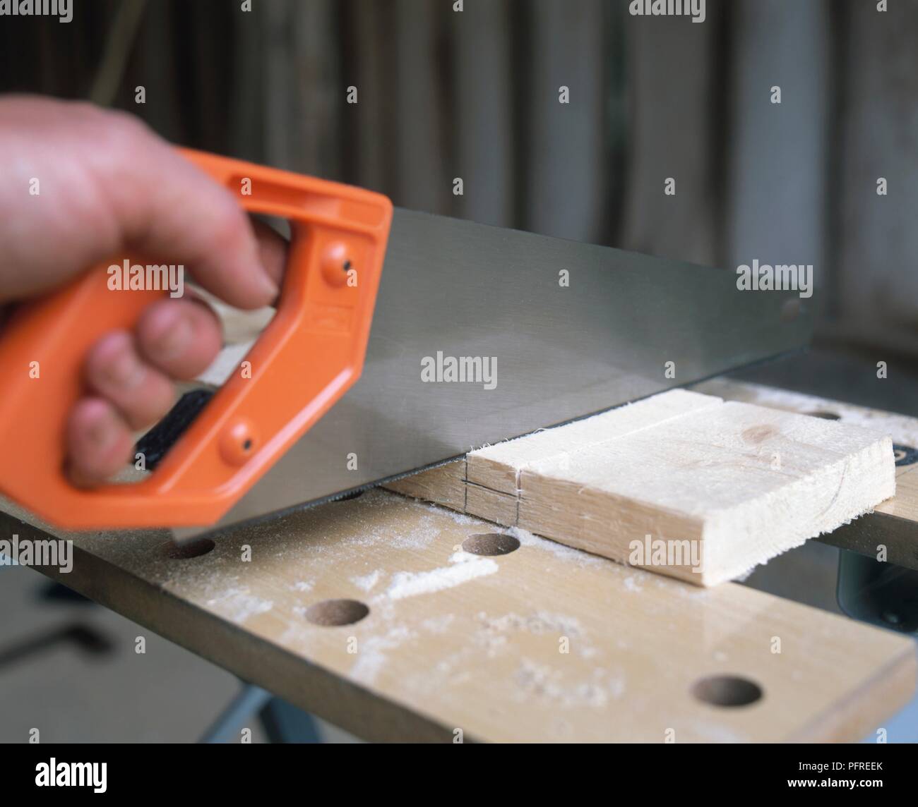 Sawing through a plank of wood, following pencilled guidelines, holding ...