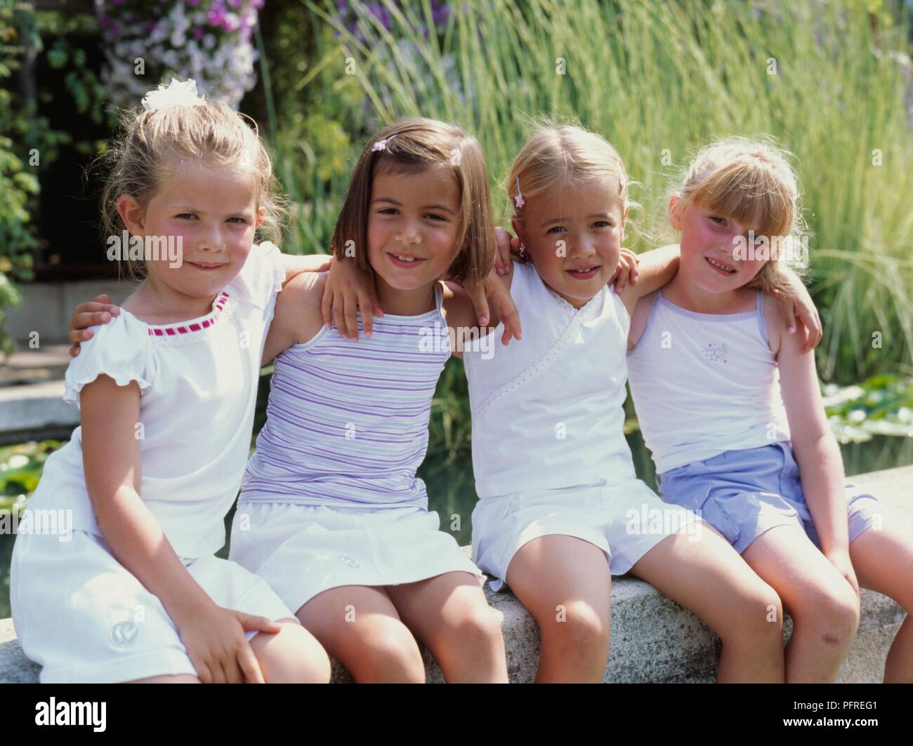 Four girls in tennis outfits sitting together with their arms around ...