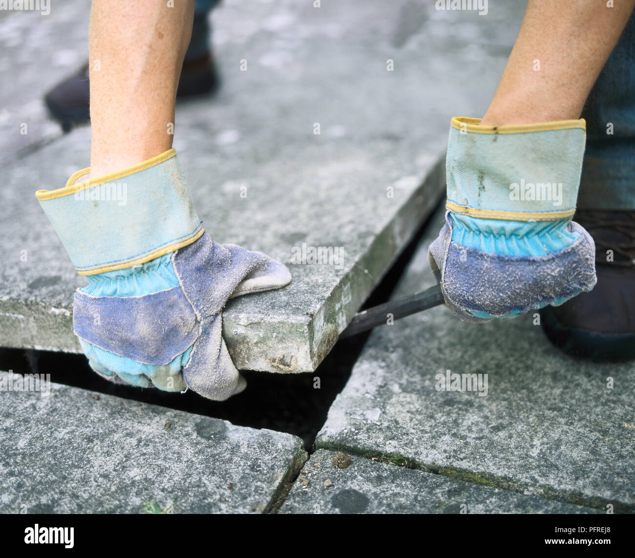 Wearing protective gloves to lift paving stone using crowbar Stock ...