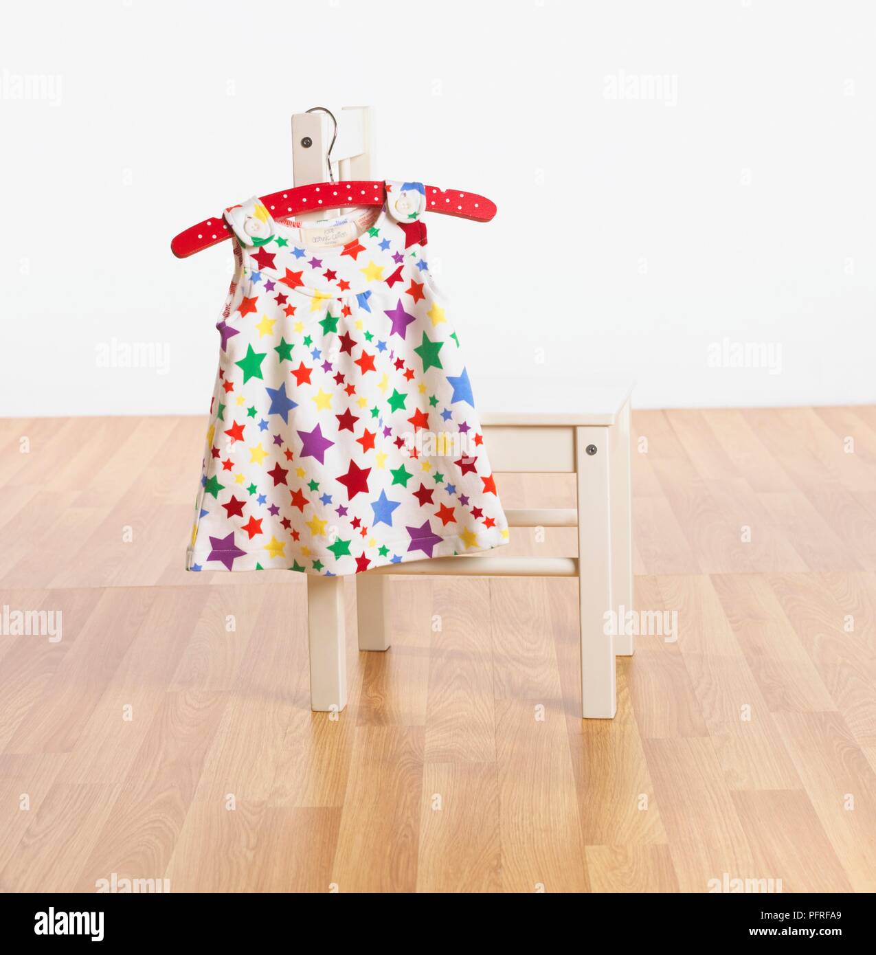 Girl's dress on clothes hanger on a chair Stock Photo - Alamy