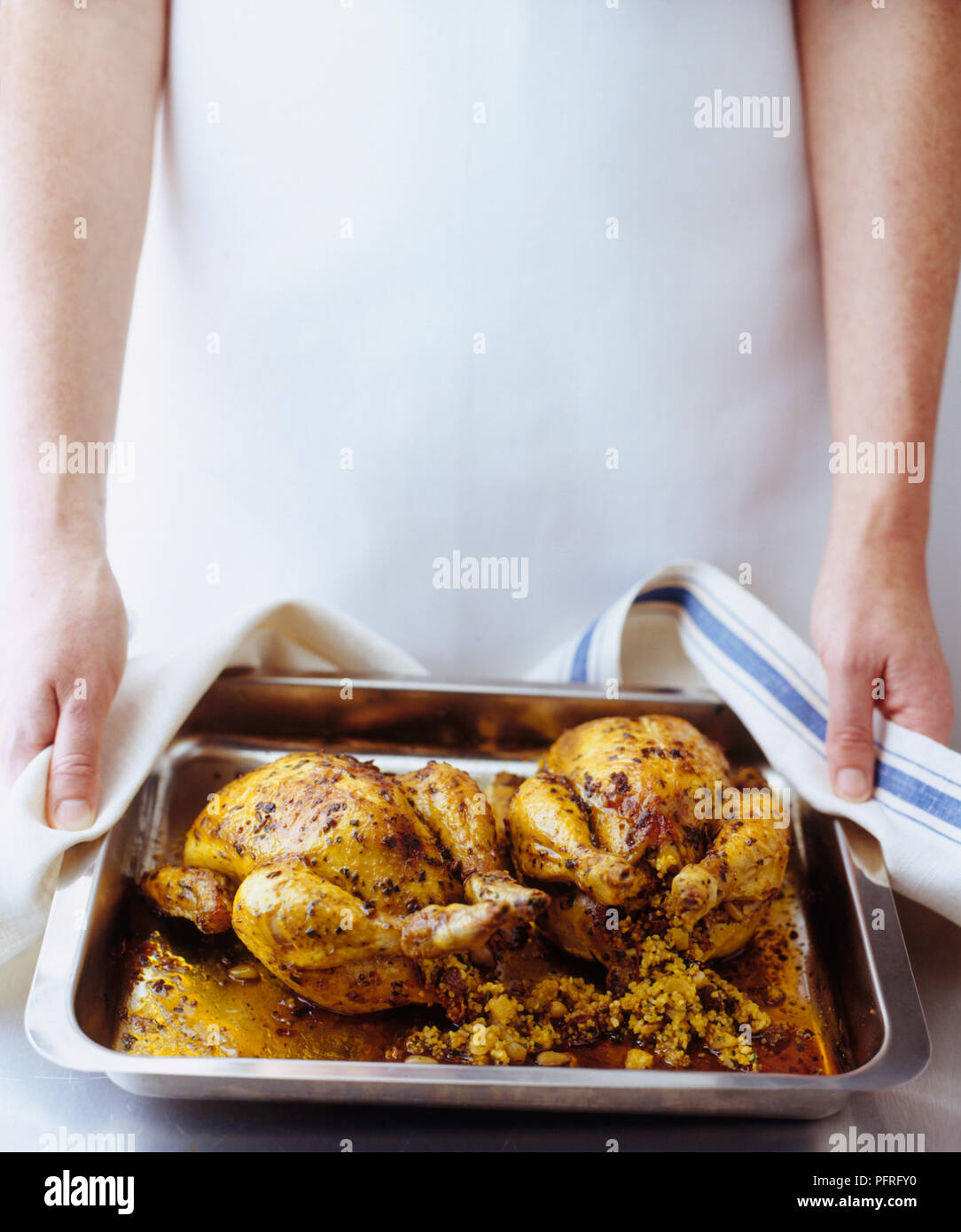 Man holding roast baby chicken with couscous stuffing in roasting tin ...