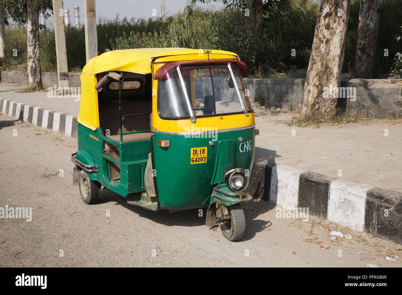 India, Delhi, green and yellow auto rickshaw next to curb on dirt road ...