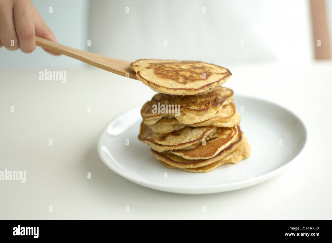 Hand holding wooden spatula placing pancake on top of pancake stack ...