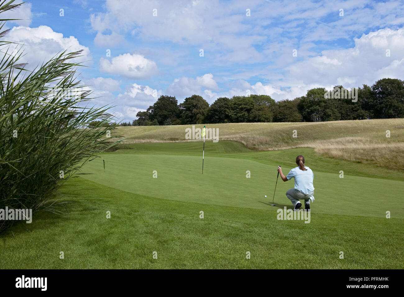 Female golfer crouching on putting green, holding golf club, ball ...