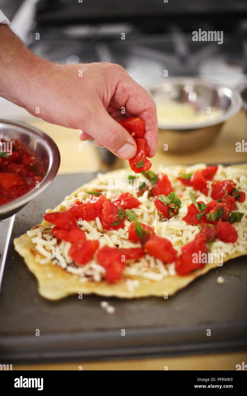 Adding tomatoes to cheese topping on grilled side of pizza base Stock ...