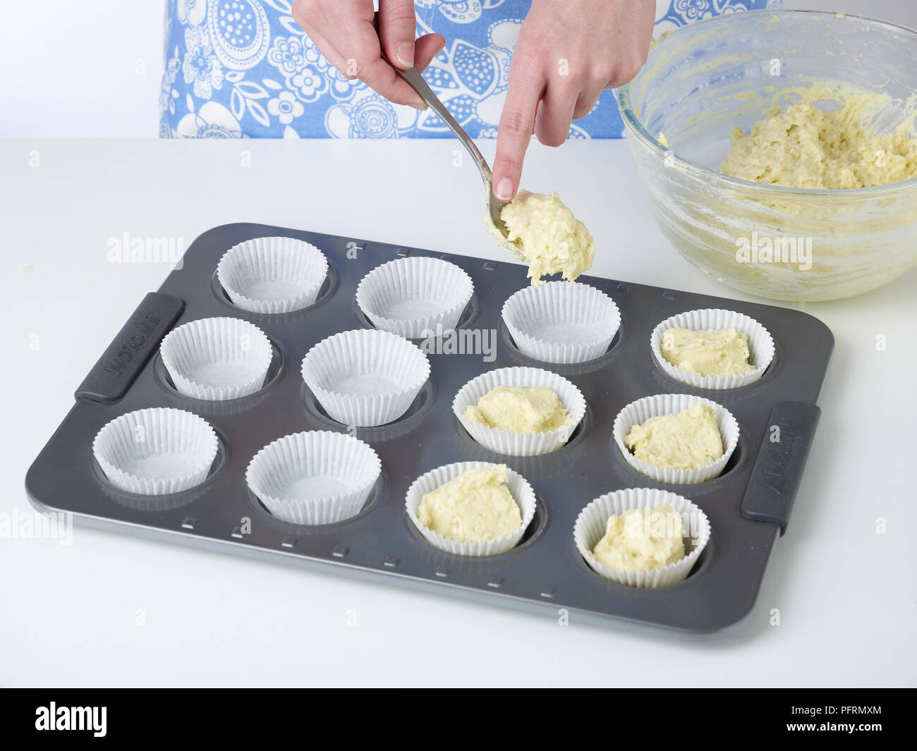 Spooning lime and coconut cupcake mixture into cake cases on a baking ...