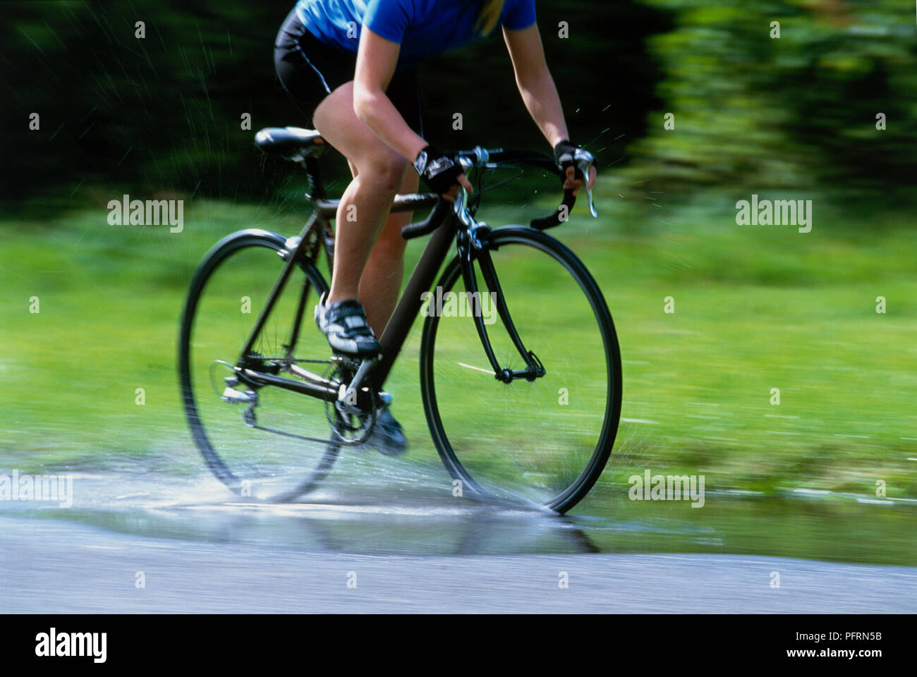 Young woman standing to riding racing bike through puddle in ...
