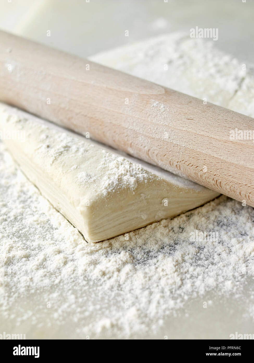 Rolling pin on top of ready made block of raw pastry on flour, close-up ...