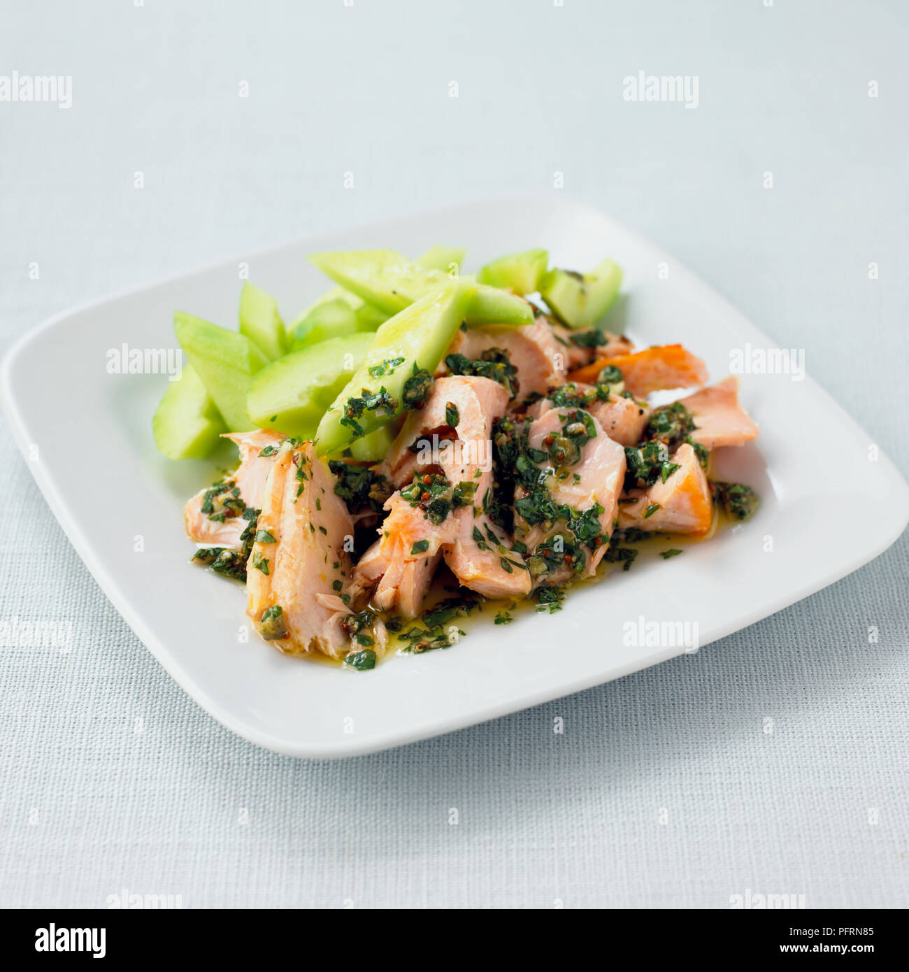 Baked salmon with salsa verde and cucumber chunks served on white plate ...