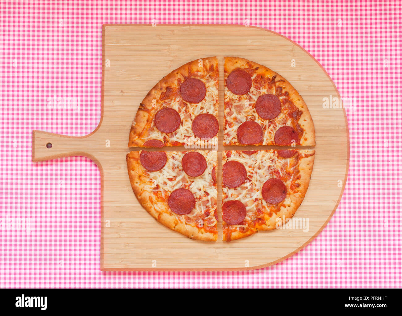 Pepperoni pizza cut into four quarters on a chopping board, against a ...