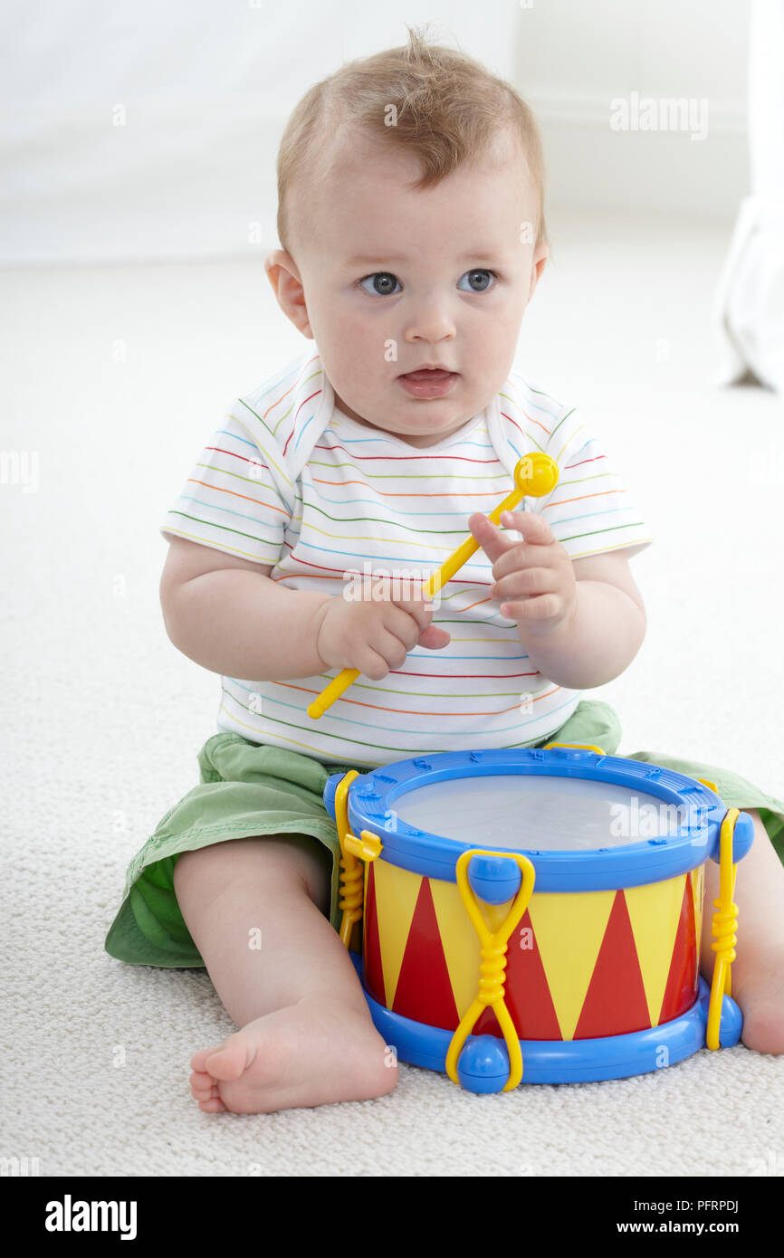 Baby boy (9 months) sitting on floor playing with a toy drum Stock ...